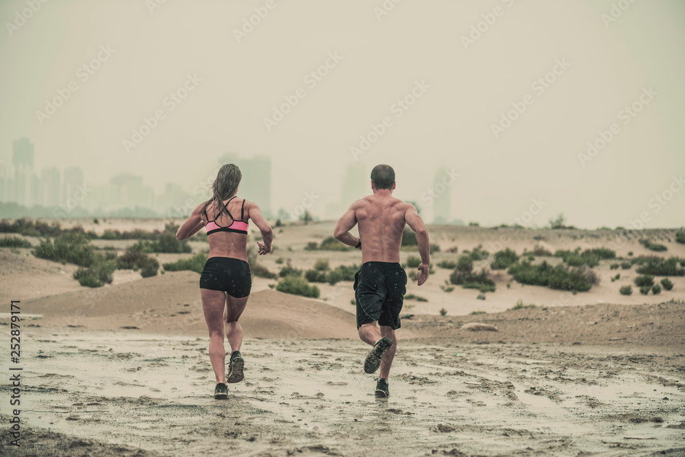 Rear view of muscular male and female athlete covered in mud running ...