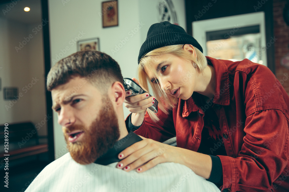 Client during beard shaving in barbershop. Female barber at salon ...
