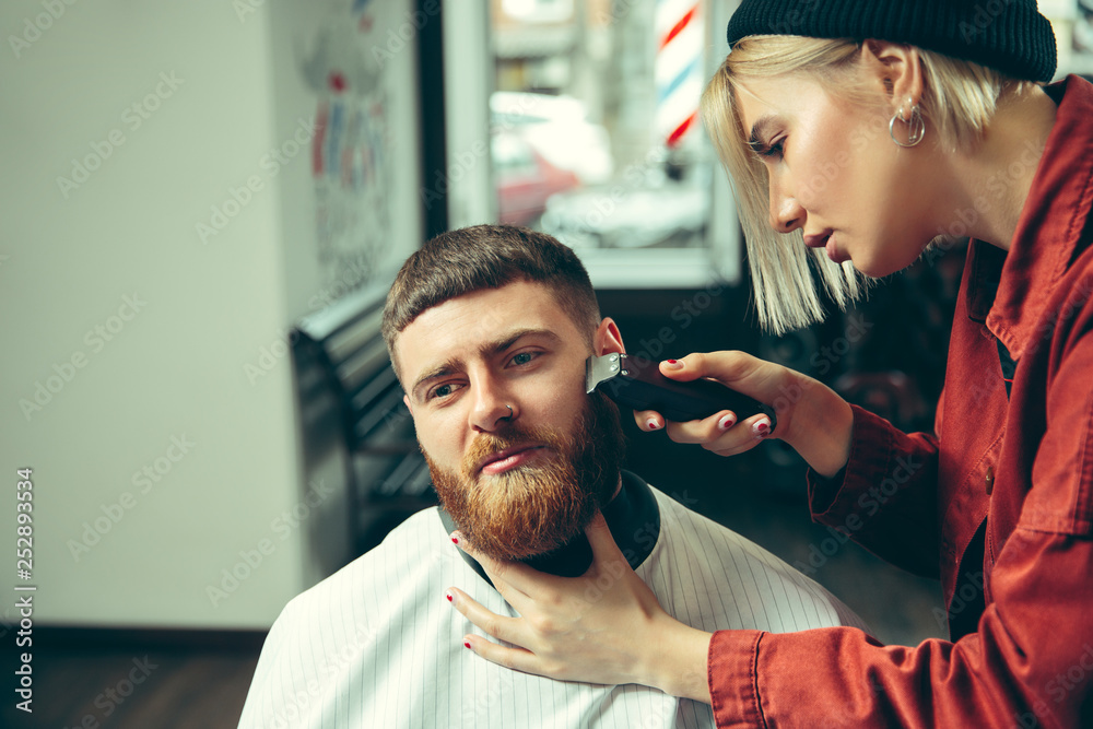 Client during beard shaving in barbershop. Female barber at salon ...