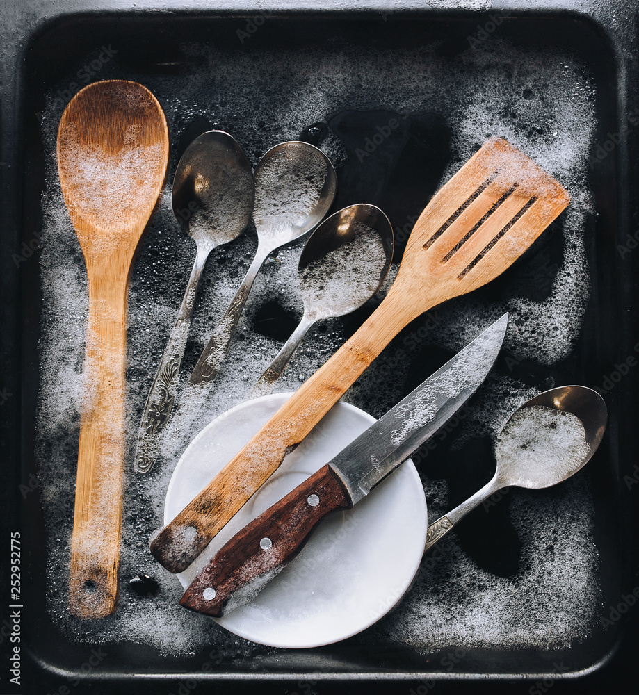 Washing dishes. A plate, a knife, wooden kitchen spatulas and spoons in ...