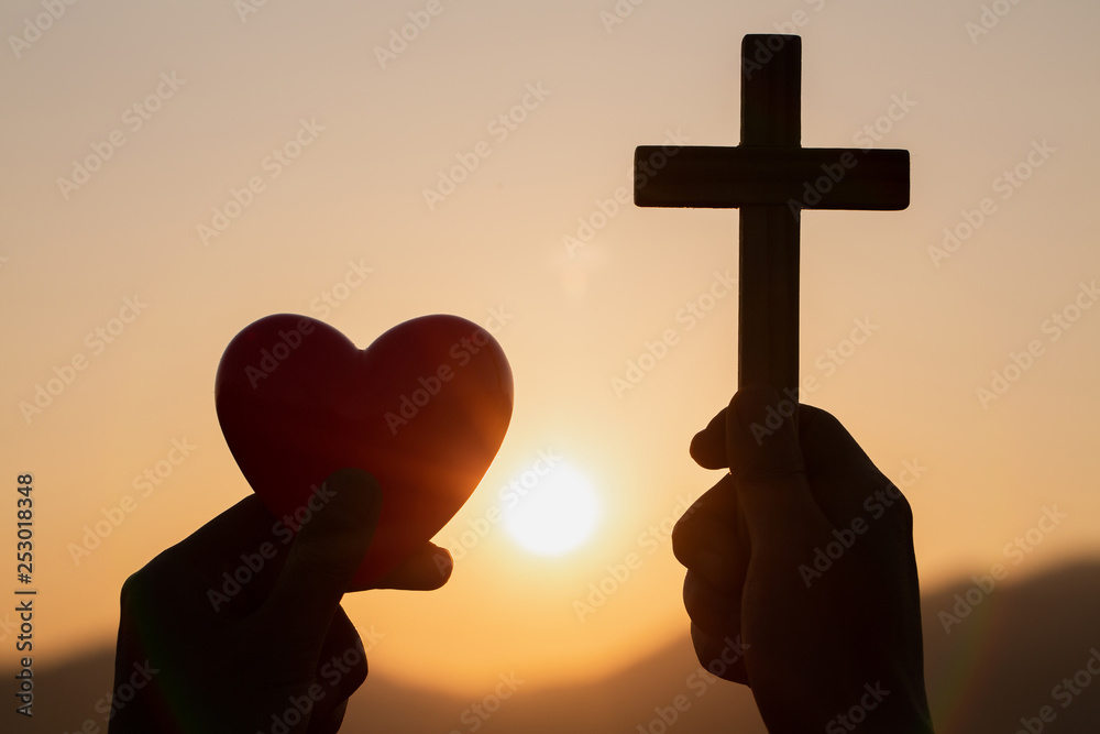 Silhouette of woman hands praying with cross and holding a red heart ...