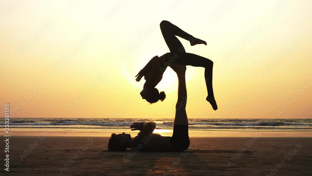 Silhouette of fit sporty couple practicing acrobatic yoga with partner ...