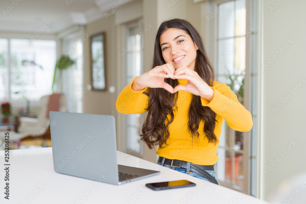 Young woman using computer laptop smiling in love showing heart symbol ...