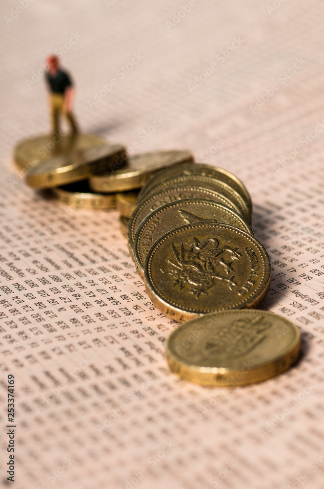 Little figure of a man climbing over tumbled one pound coins laid over ...