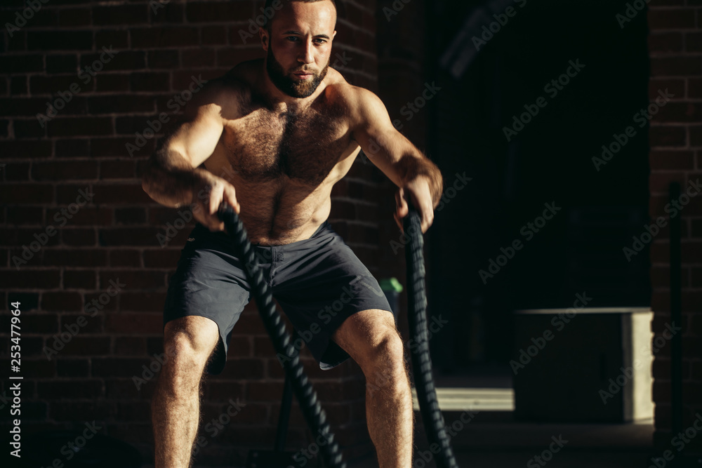 Athletic young man with battle rope doing exercise in functional ...