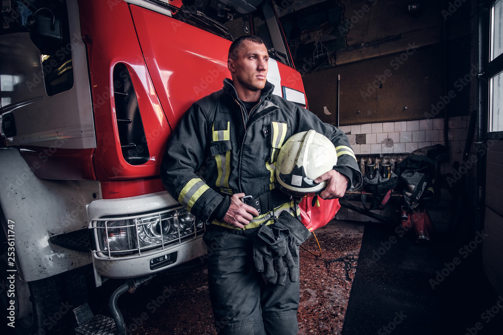 Portrait of a brave young fireman wearing uniform holding a helmet and ...
