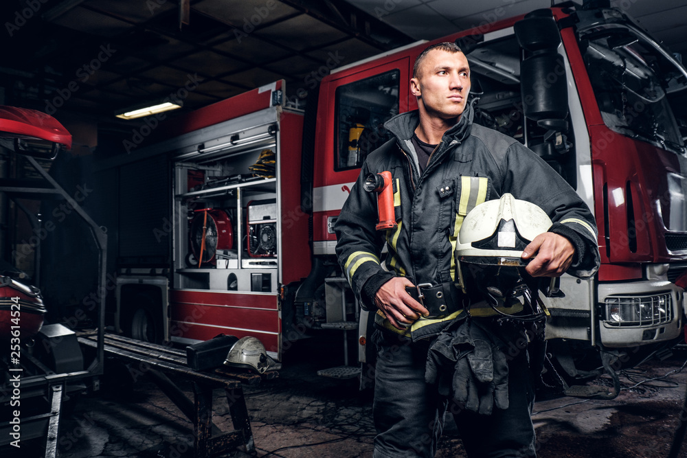 Fireman wearing uniform holding a helmet and looking at a camera while ...