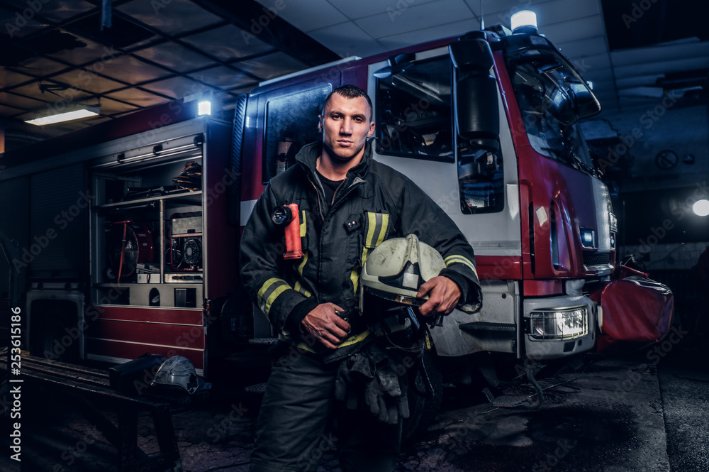 Handsome fireman wearing uniform holding a helmet and looking at a ...
