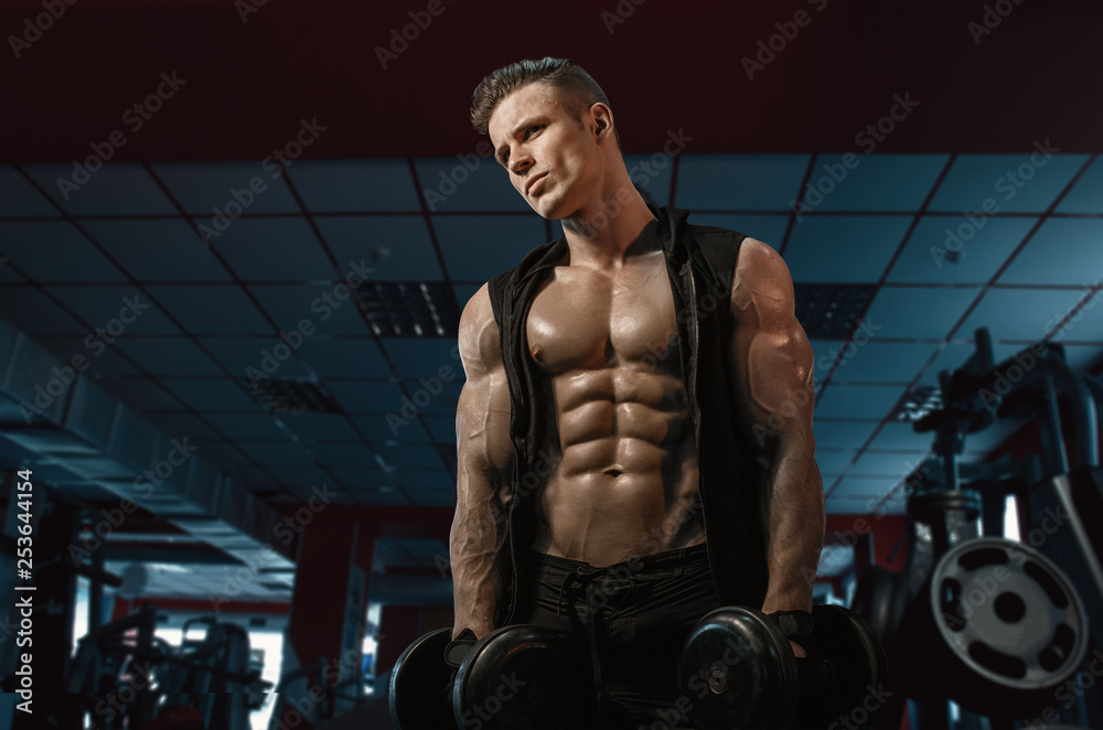 Muscular model sports young man exercising in gym with dumbbell ...