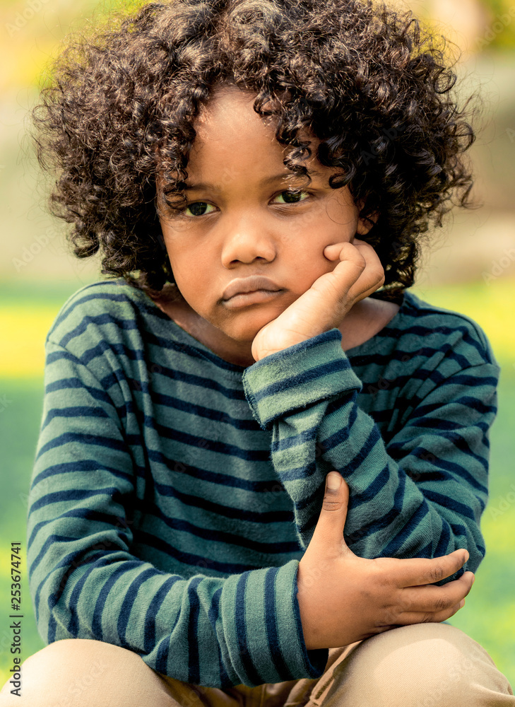Unhappy bored little african american kid sitting in the park. The boy ...