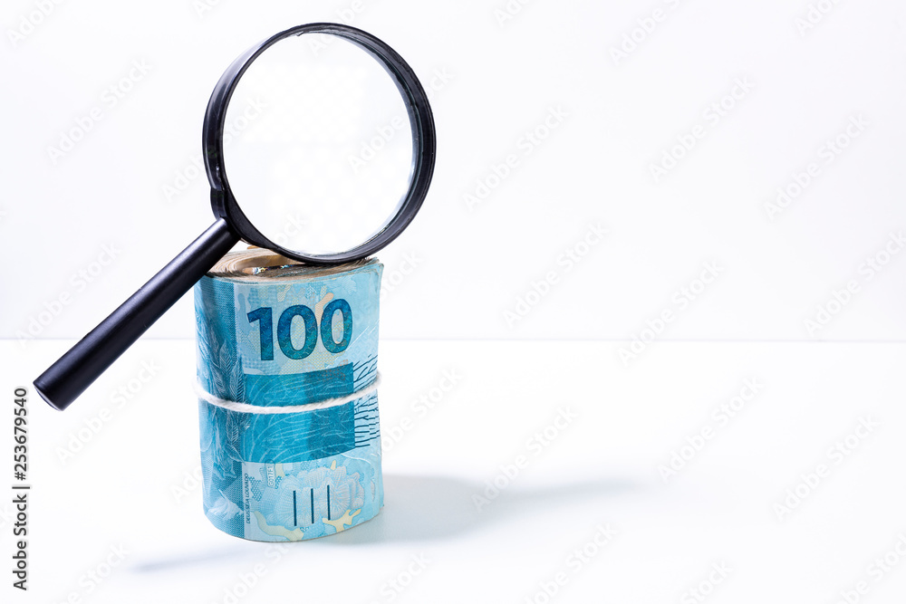 Thick roll of banknotes beneath a magnifying glass lit from behind ...