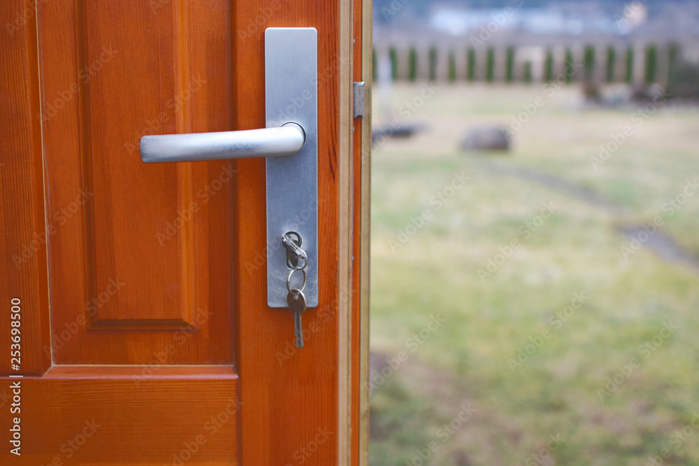 Open wooden door with keys in keyhole on defocused landscape background ...