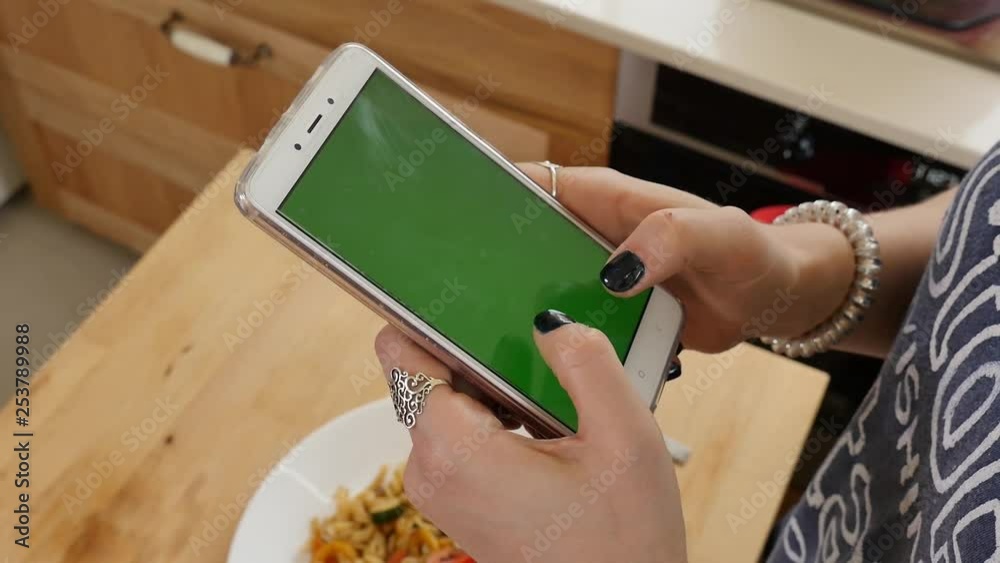 Close up of woman hands texting on smartphone in the kitchen. Green ...