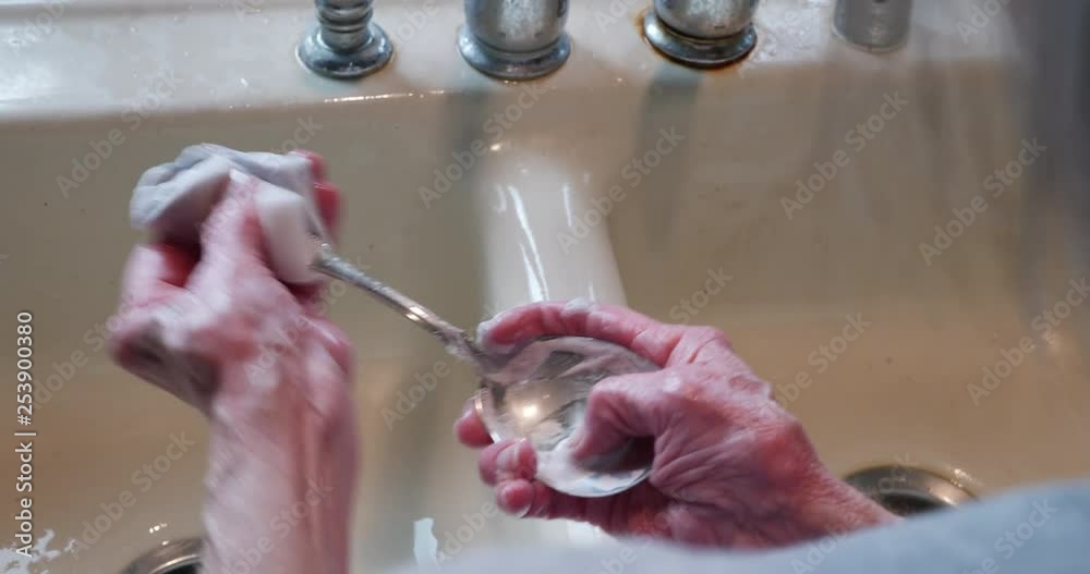 The wrinkled hands of an old woman polishing a piece of silverware in ...