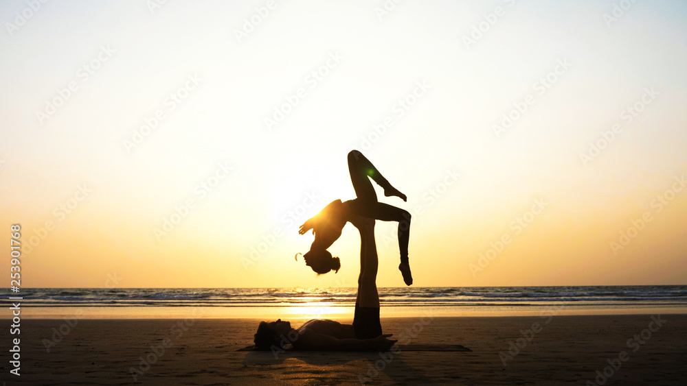 Silhouette of fit sporty couple practicing acrobatic yoga with partner ...