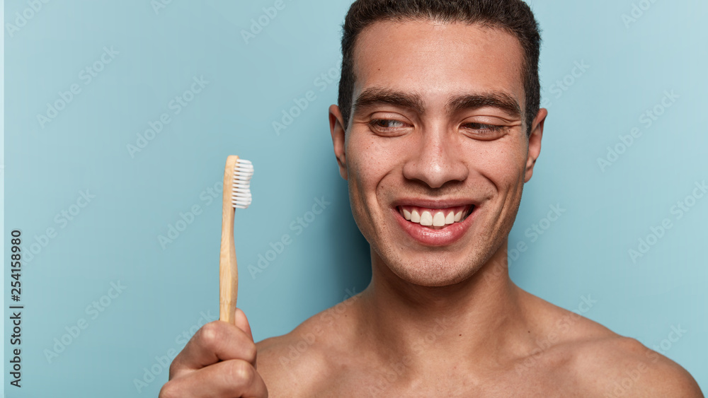 Cheerful muscular young man holds toothbrush, has shining smile ...