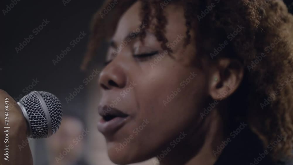 Close up side view of one young African female singer singing and ...