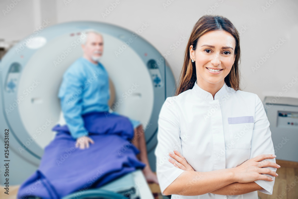 Portrait smiling doctor, standing at medical room with CT scan. Behind ...