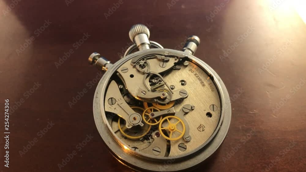 Mechanical stopwatch with exposed gears on mahogany. Close up pan of ...