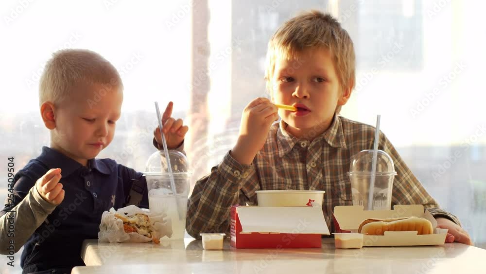 Children have lunch in fast food cafe. Boys drink lemonade and eat ...