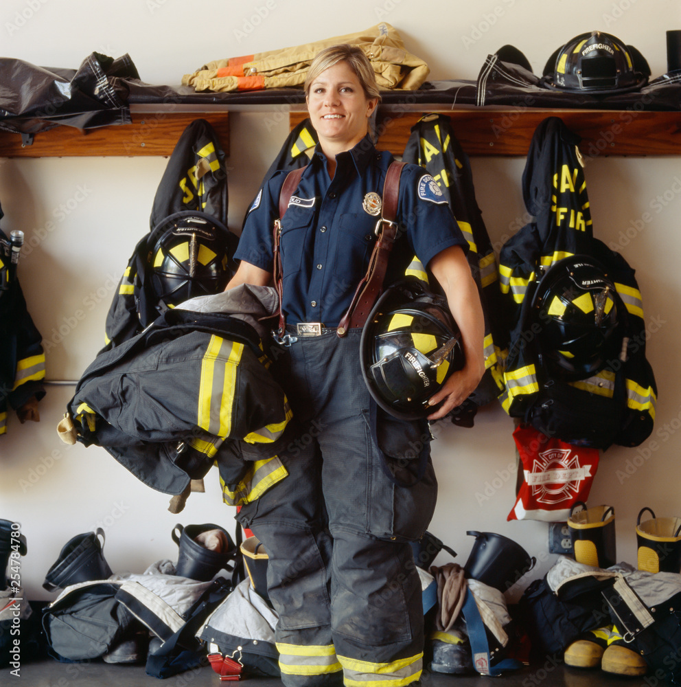 Portrait of female firefighter with helmet standing in fire station ...