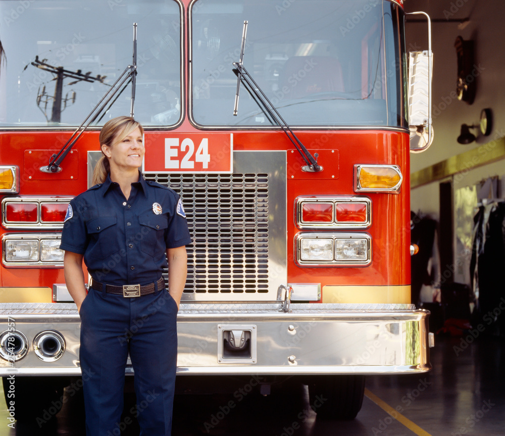 Smiling female woman firefighter in uniform with fire engine truck at ...