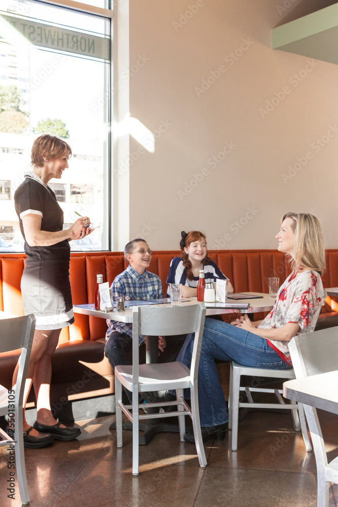 Friendly, smiling waitress server in uniform taking order from family ...