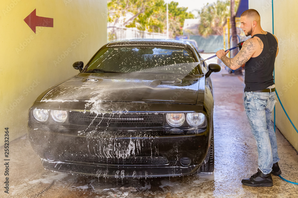A worker slowly rinses the front of a black car at the car wash. The ...