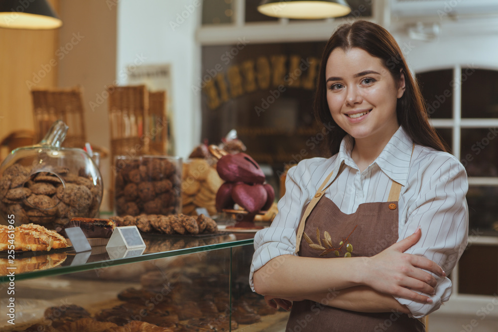 Charming young female baker smiling to the camera, posing proudly at ...
