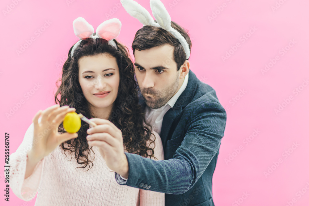 Happy Easter Young couple on pink background. On the head is a bunny ears. The wife holds a ...