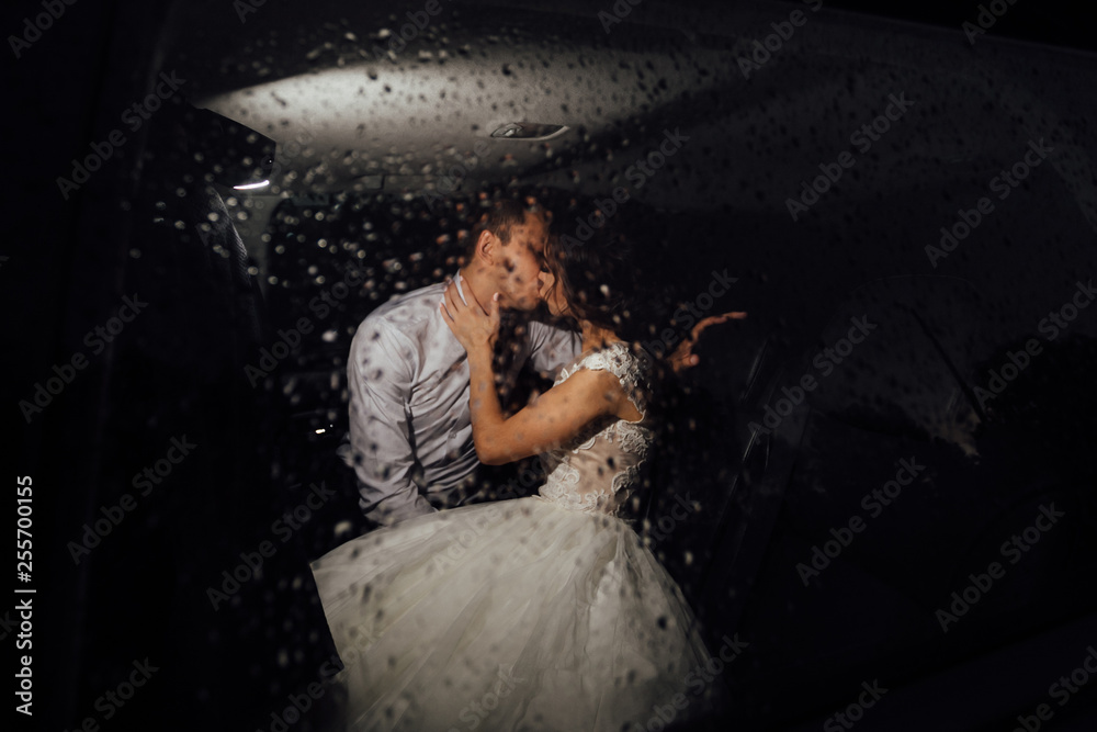 The bride and groom kissing in the car late at night, and it's raining ...