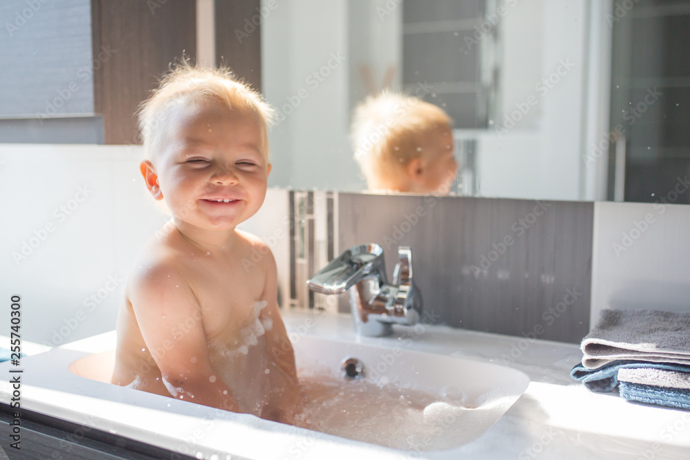 Baby taking bath in sink. Child playing with foam and soap bubbles in ...