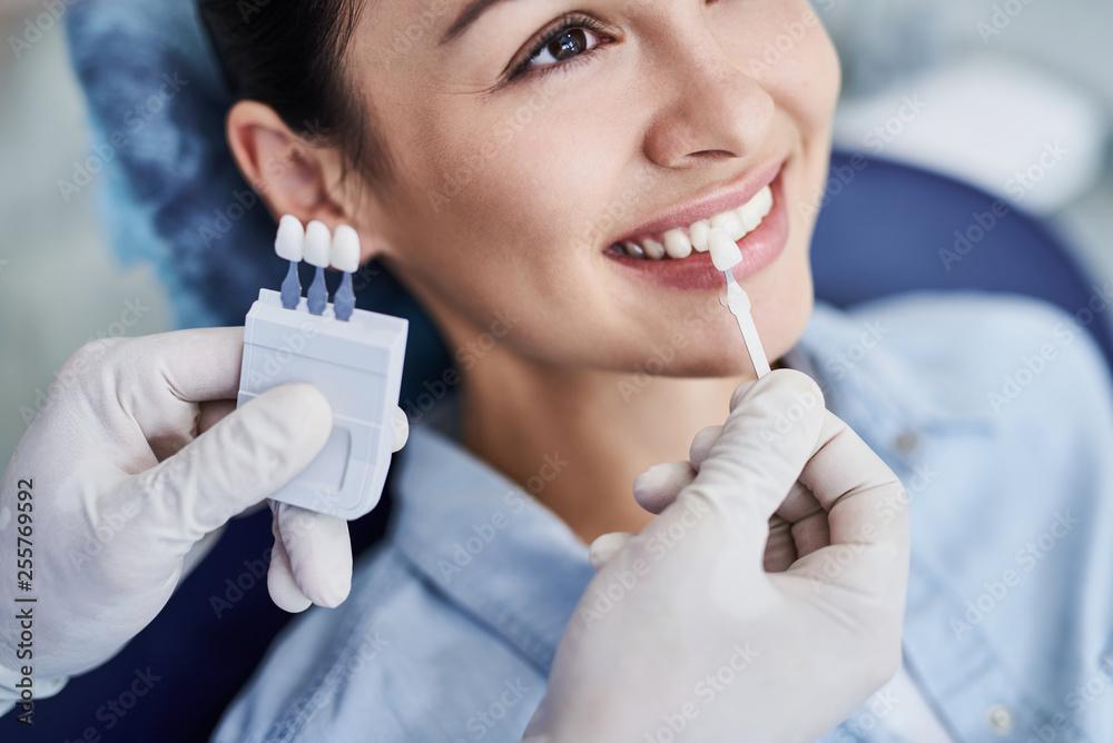 Dentist in sterile gloves comparing color of lady teeth with sample ...