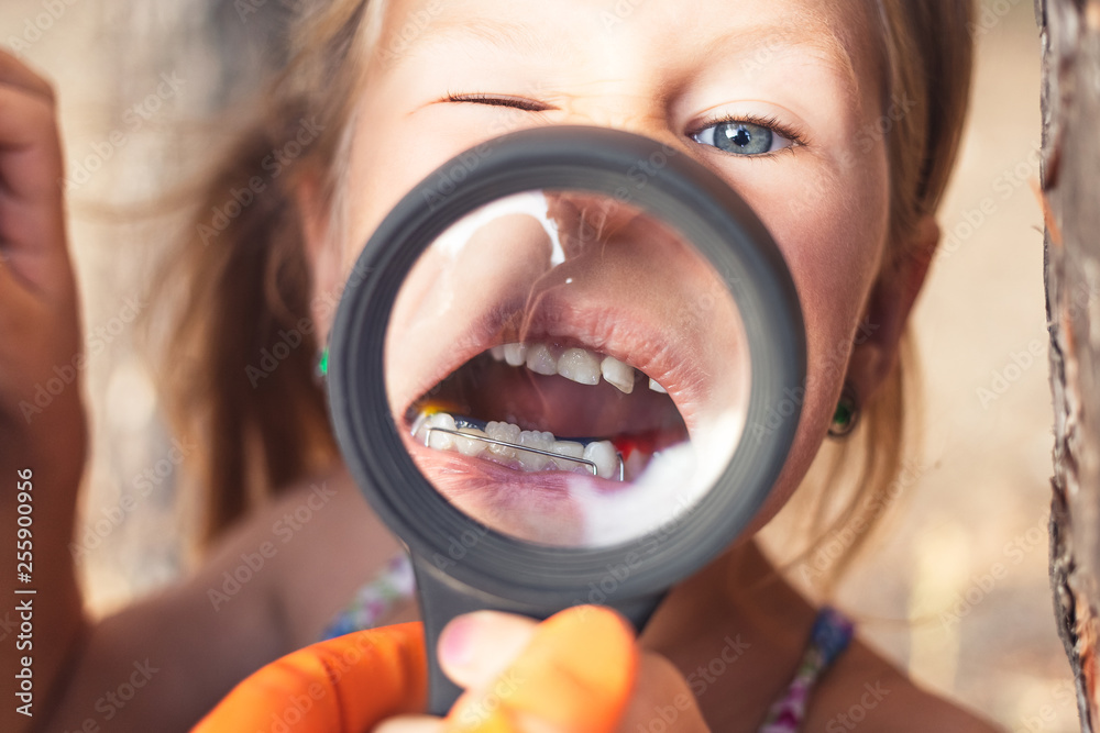 A little girl put a magnifying glass to her mouth to show an ...