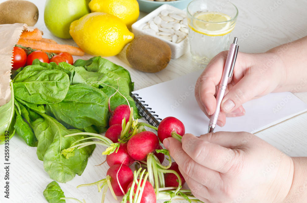 Woman writing her meal and diet plan. Fresh fruits, vegetable and seeds ...