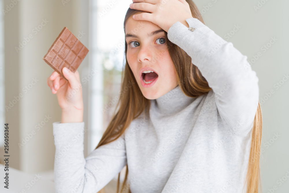 Beautiful young girl kid eating chocolate bar stressed with hand on ...