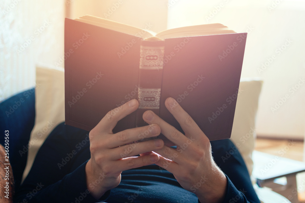 Man lies in bed and holding open book. Male hands hold open book ...