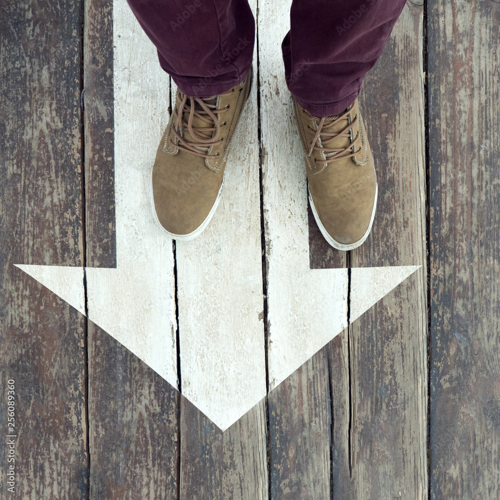 White arrow sign on wooden floor. Man's legs standing on arrow sign ...