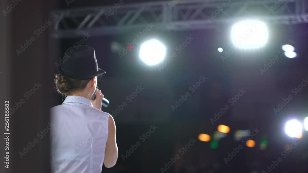 Singing girl. Back view of girl singer in stage lights. Young stylish ...