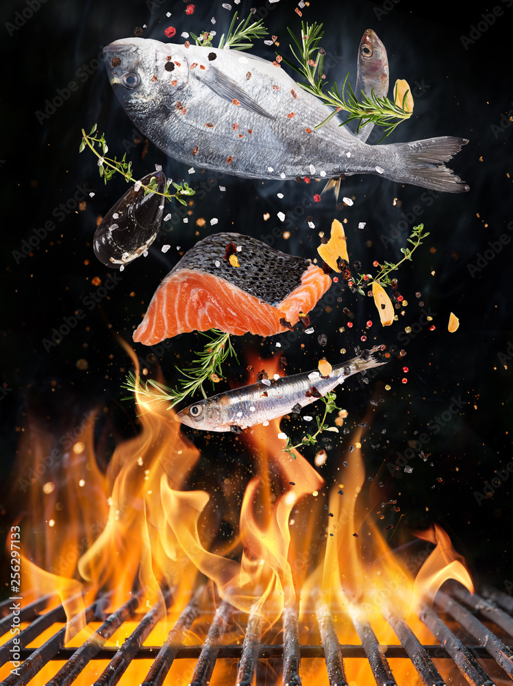 Tasty fishes flying above cast iron grate with fire flames. Freeze ...