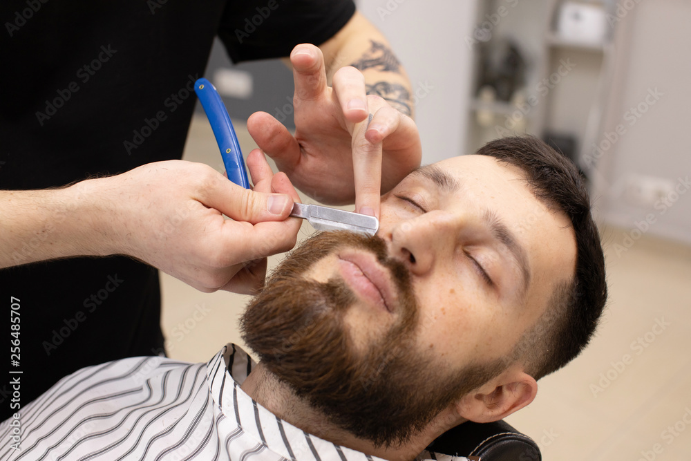 Shaving process of beards in Barbershop. Master makes a haircut beard ...