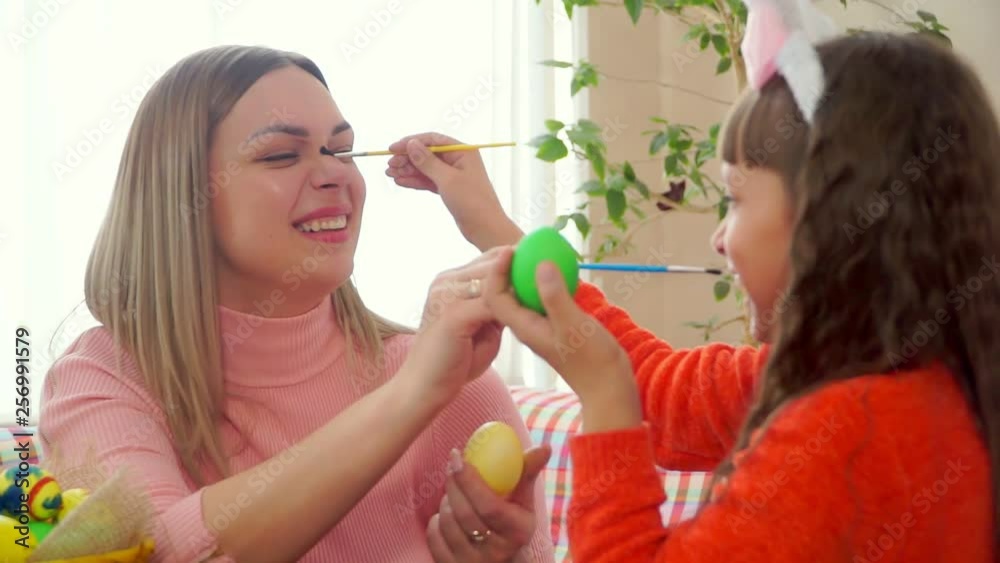 close - up mom and daughter paint Easter eggs, and then brushes tickle ...