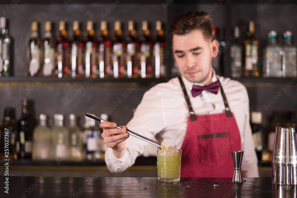 Bartender finishes decoration of his cocktail with ice cubes and lime ...
