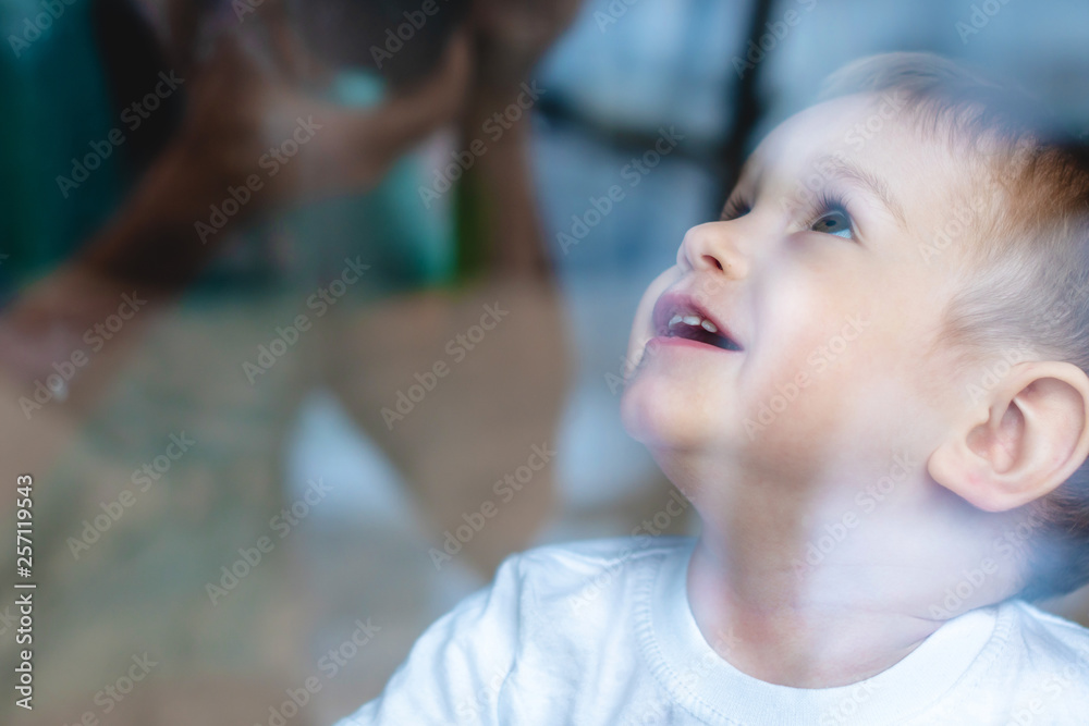 Cute baby boy looking in the window glass. Loneliness of children and ...