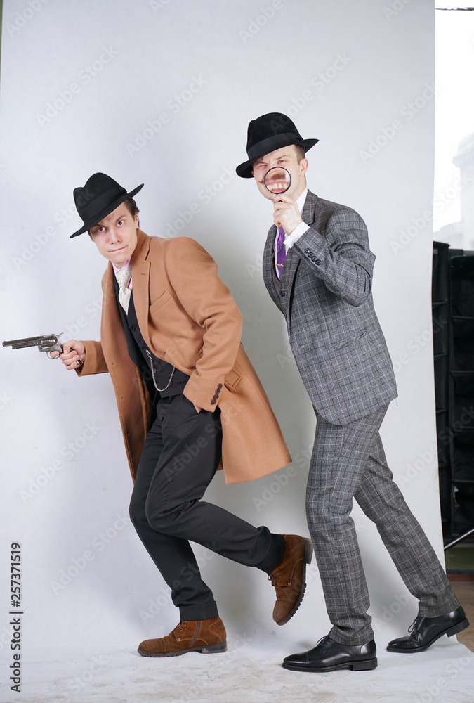 two caucasian detective men in retro suits with vintage hats sneak ...