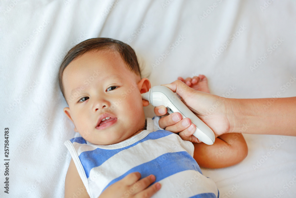 Mother takes temperature for infant with ear thermometer on bed at home ...