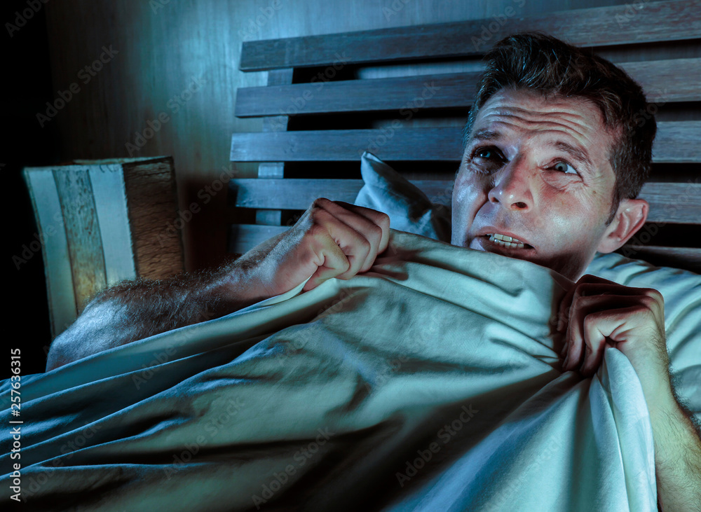 sleepless young man lying in bed stressed and scared suffering ...