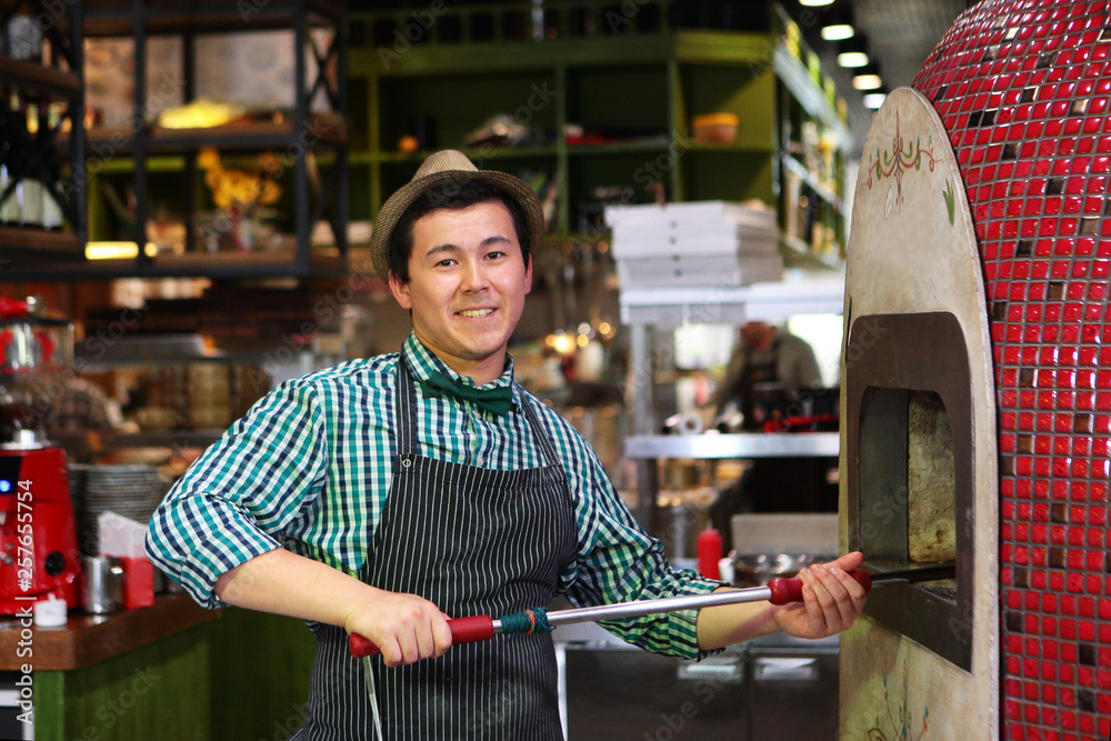 Foto de A young guy, an Asian-looking pizza maker places the finished ...