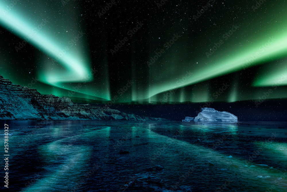 iceberg floating in greenland fjord at night with green northern lights ...