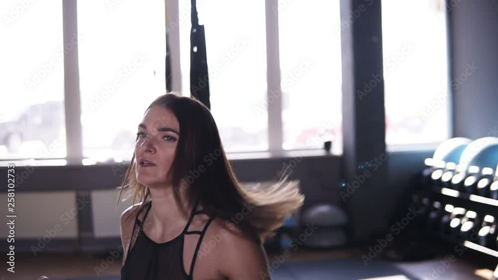 Young sporty woman is training muscles of hands and back using rubber ...